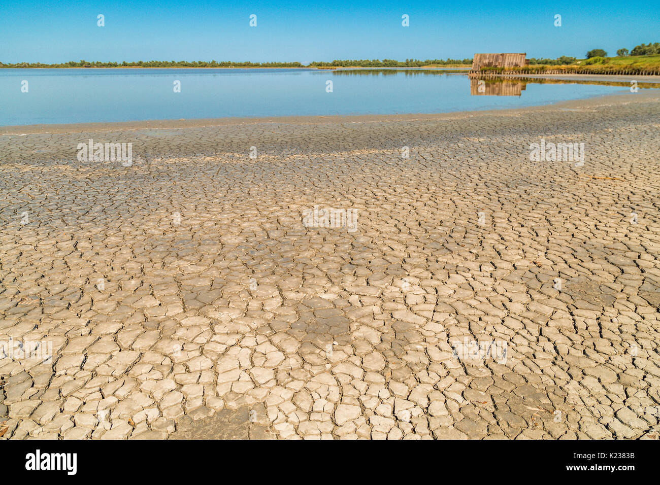 cracked clay soil beach with a straw hut on clear lagoon water Stock ...