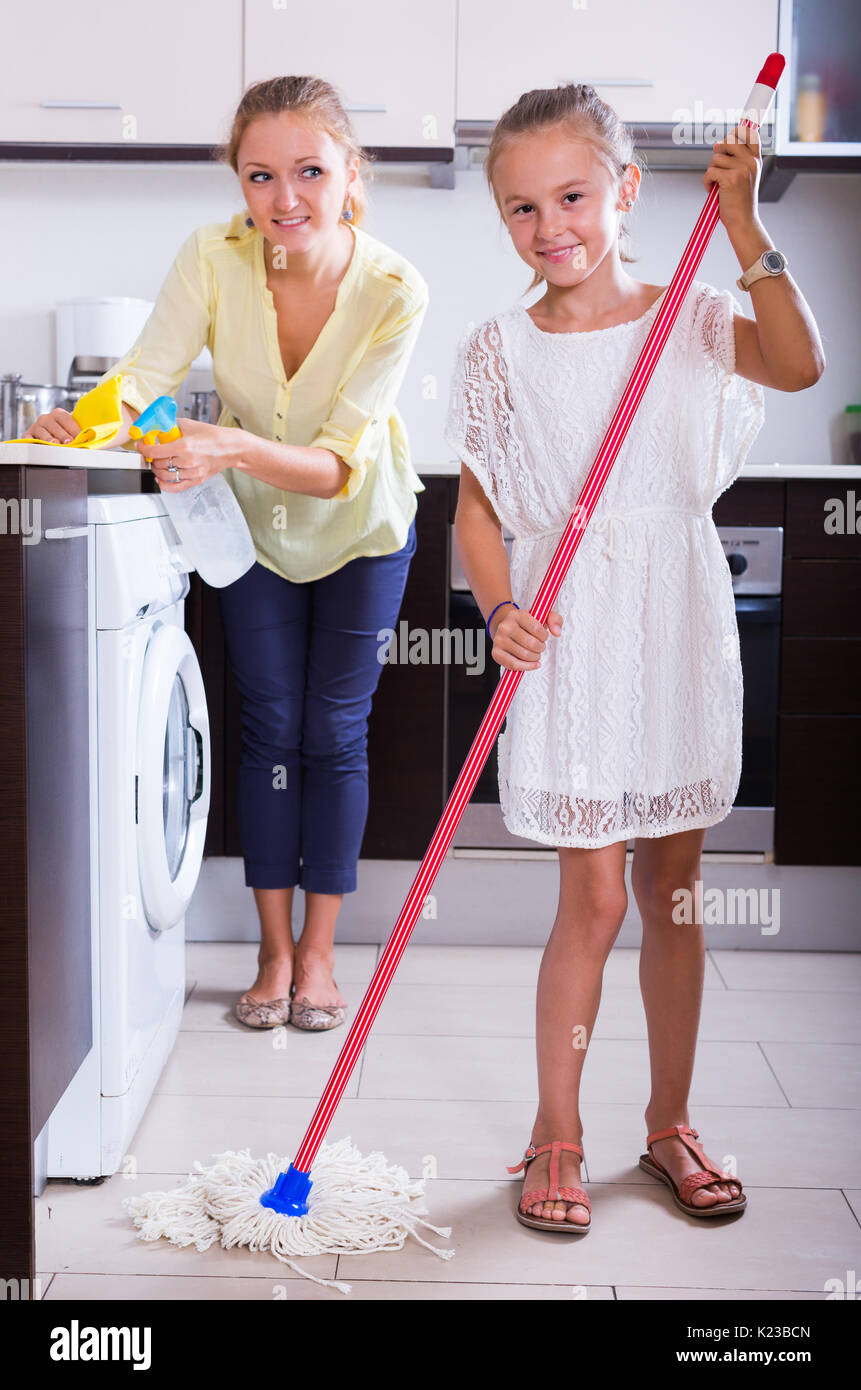 Diligent little girl helping joyful smiling mother clean up in the ...