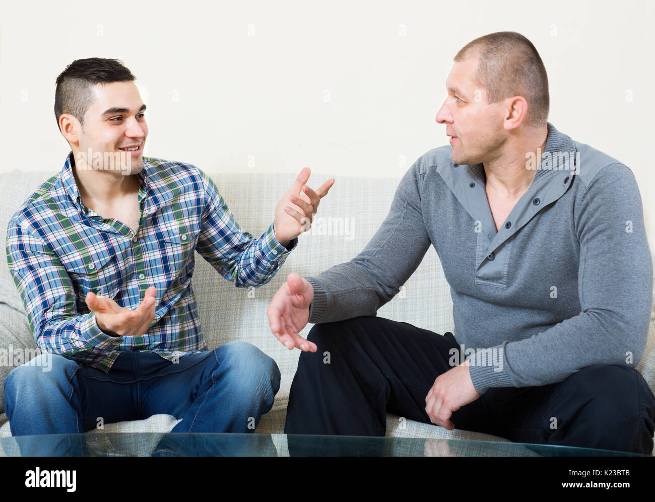 Two male friends sitting on sofa and talking at home Stock Photo - Alamy