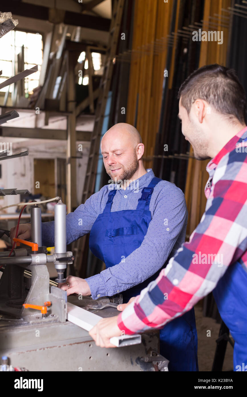 Two joyful workers in uniform working on a machine in PVC shop Stock ...