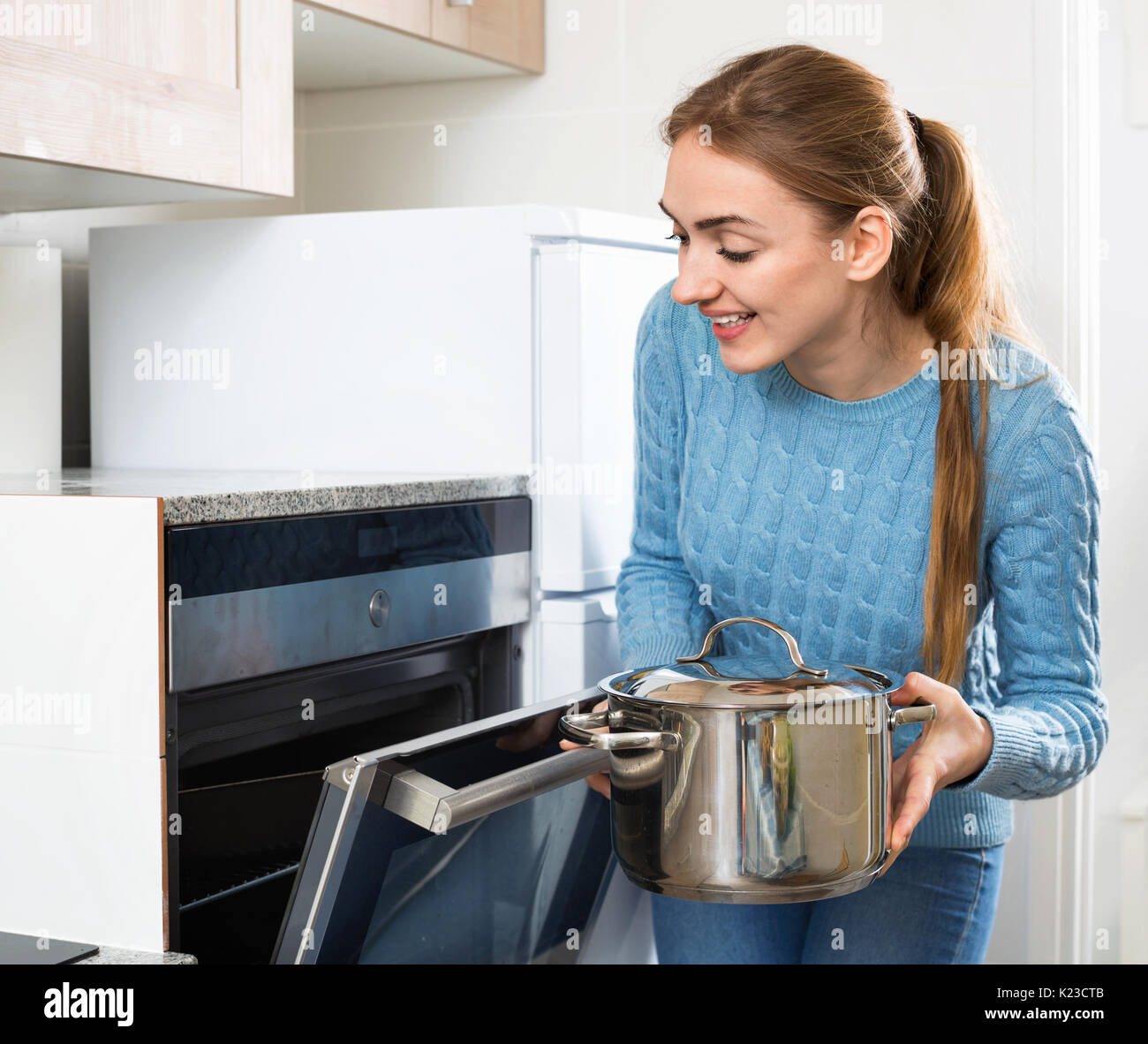 Portrait of happy positive girl putting pan in kitchen oven smiling ...