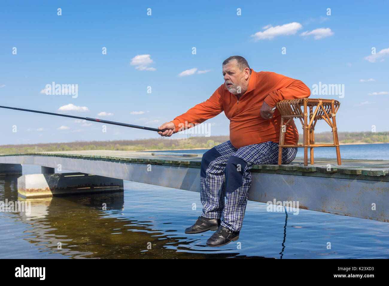 Elderly fisherman sitting on a pier with rod and ready to catch fish ...