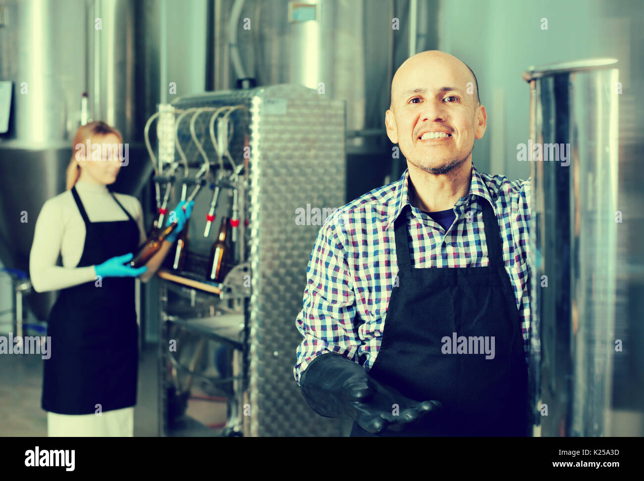 Mature cheerful man wearing a uniform standing among the brewery ...