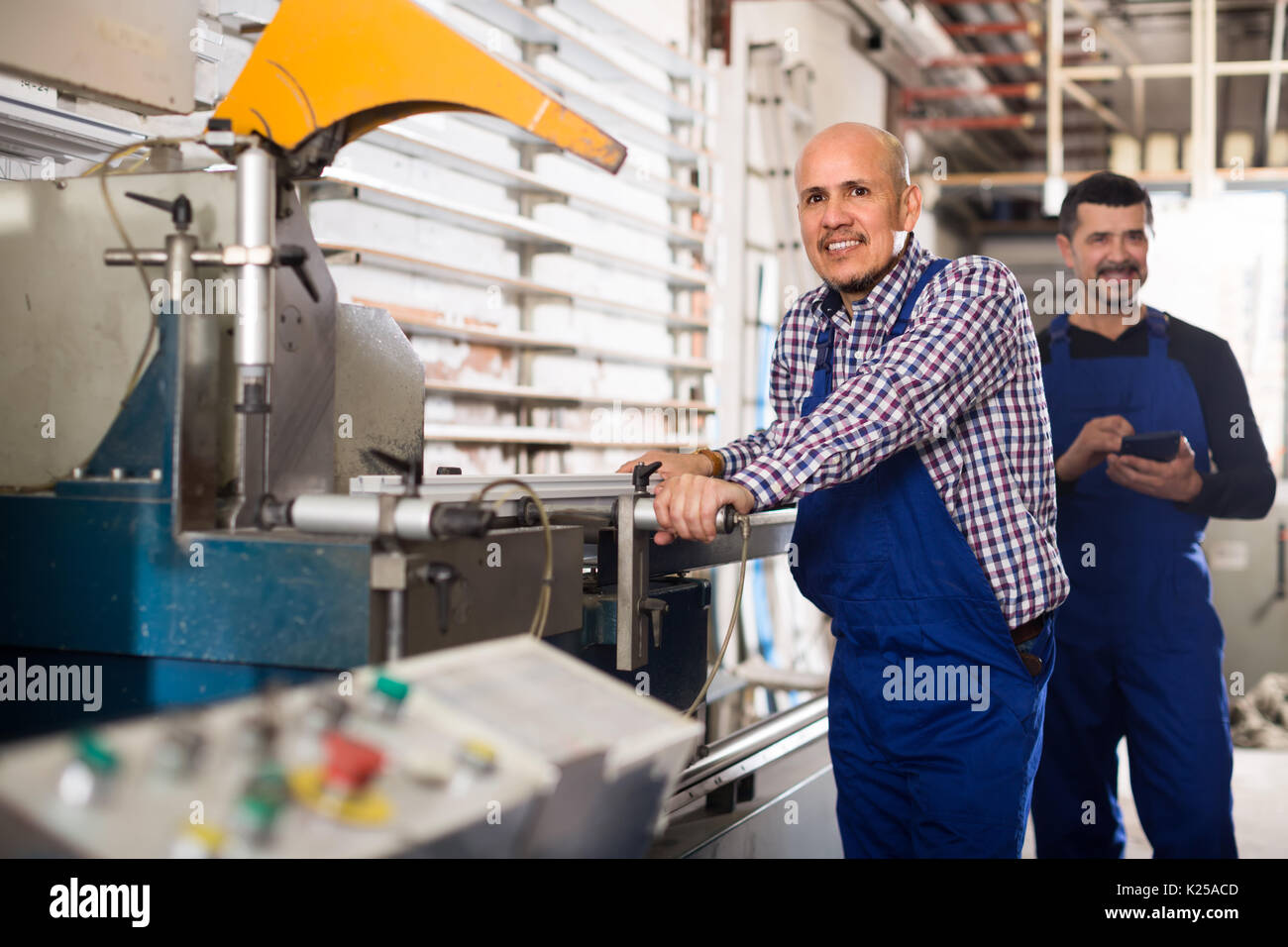Two smiling workmen in overalls near cutter - lathe machine at factory ...