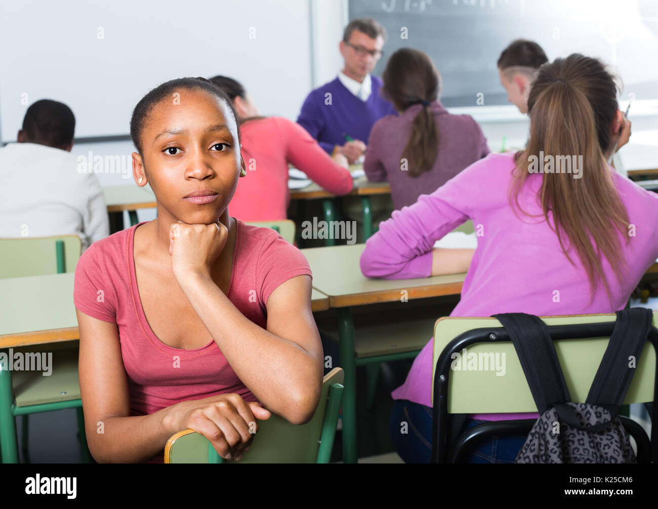 Portrait of a sad student girl sitting lonely while others listening ...