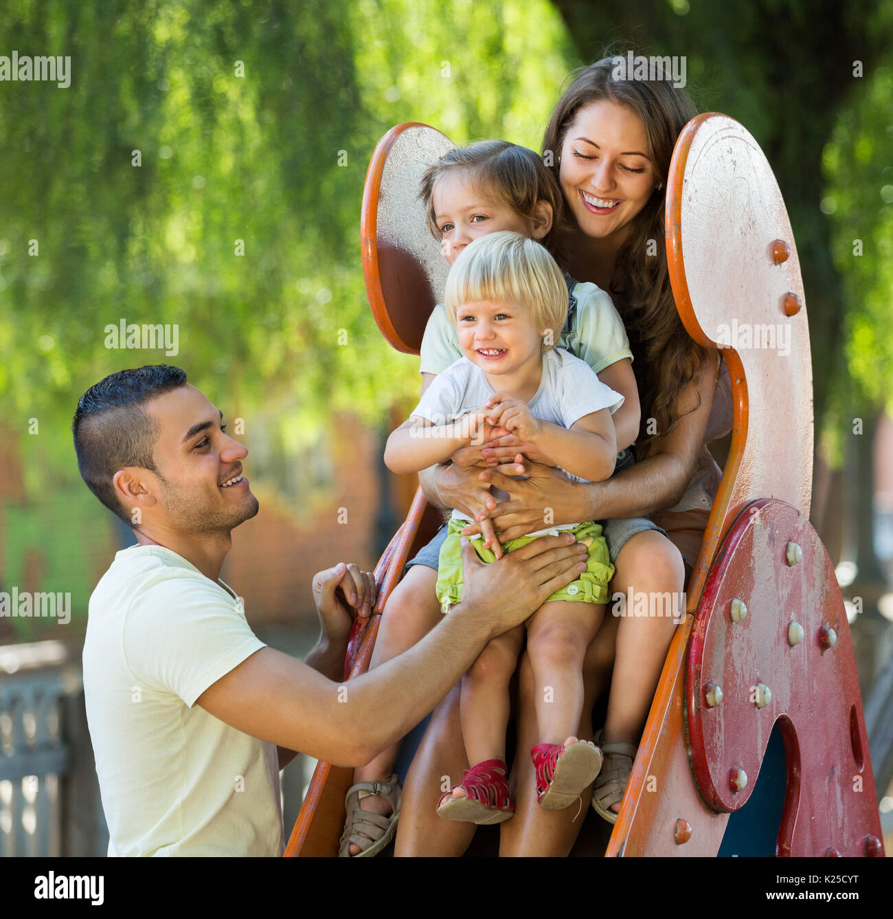 Smiling people helping kids on slide in summer day Stock Photo - Alamy