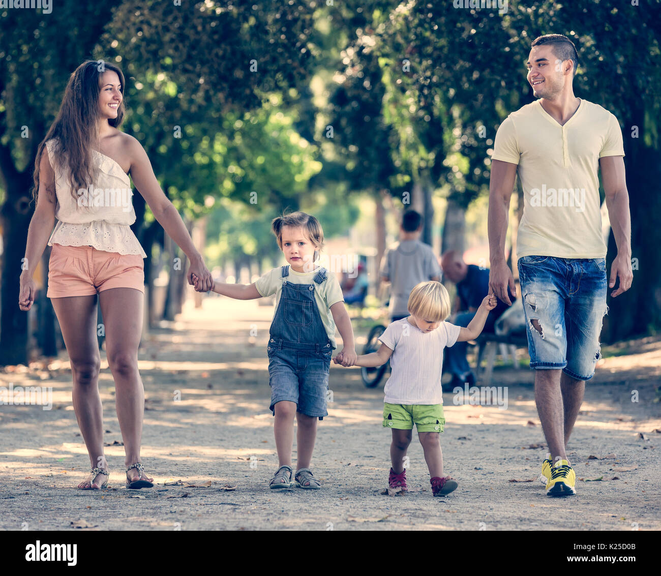 European family with two little children walking in park on sunny day ...
