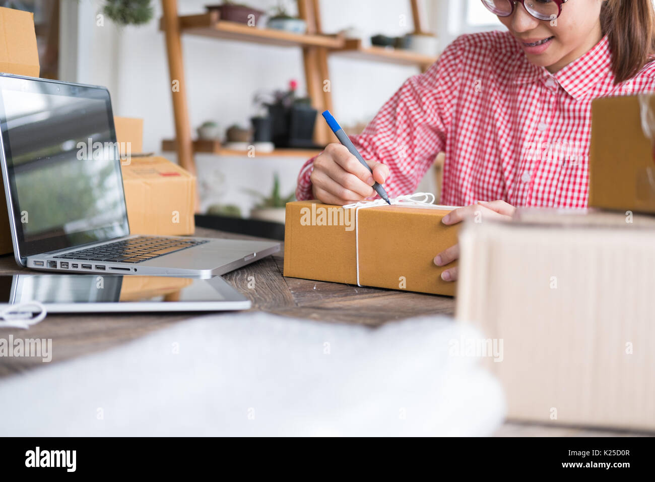 young start up small business owner writing address on cardboard box at ...