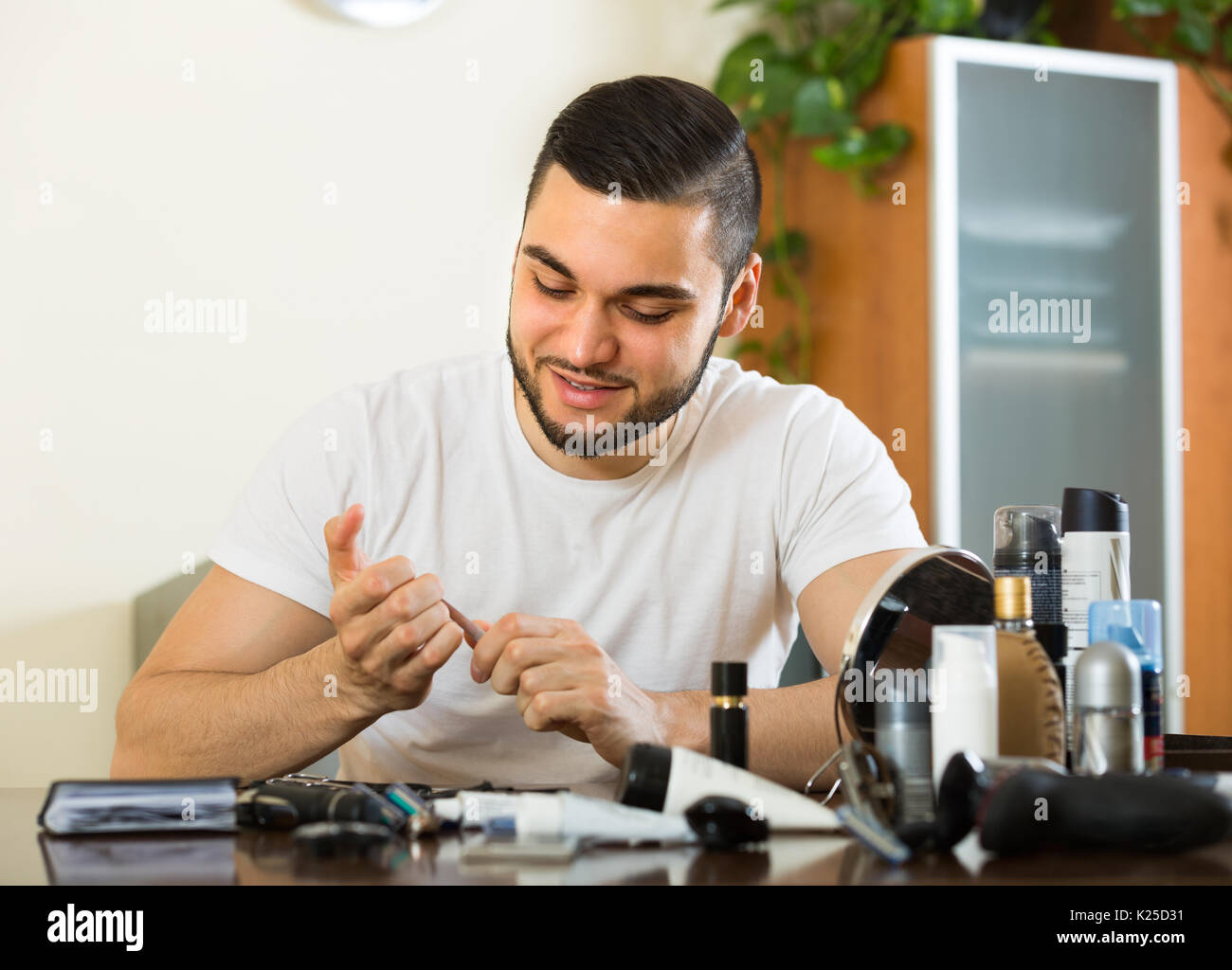 Handsome young guy cutting nails with cuticle scissors in home interior ...