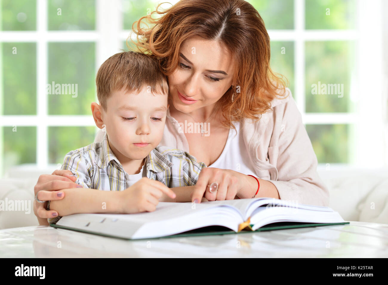 Mother and son doing homework together reading book Stock Photo - Alamy
