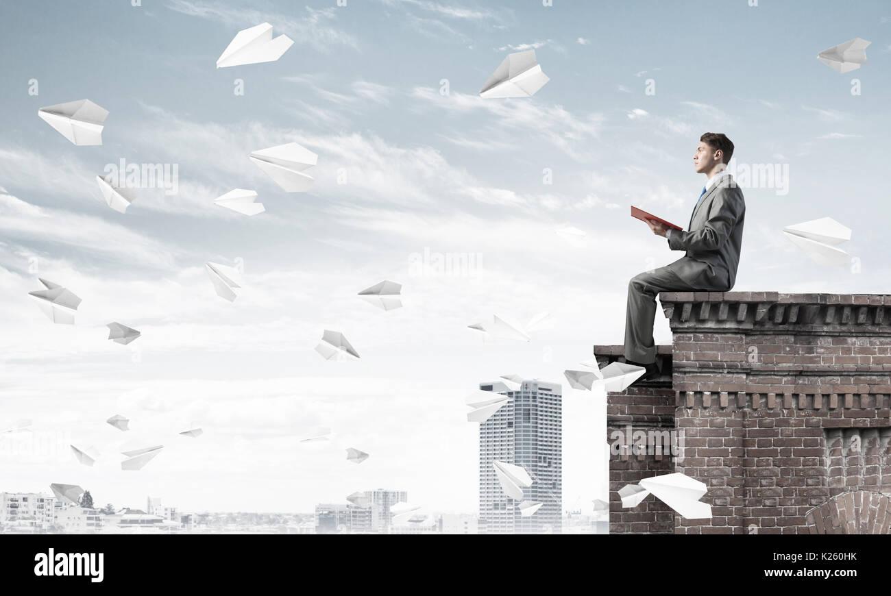 Man on roof edge reading book and cityscape at background Stock Photo ...