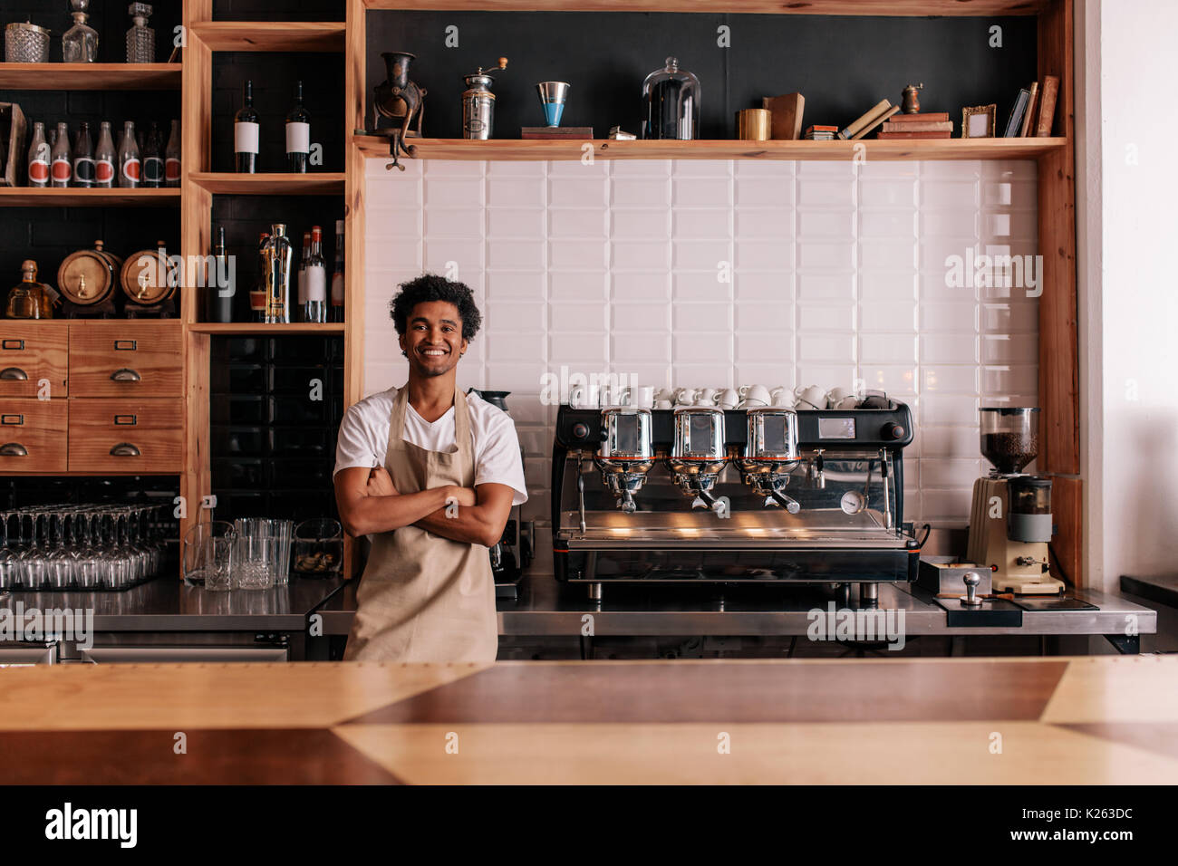 Portrait of confident young man wearing apron standing behind cafe ...
