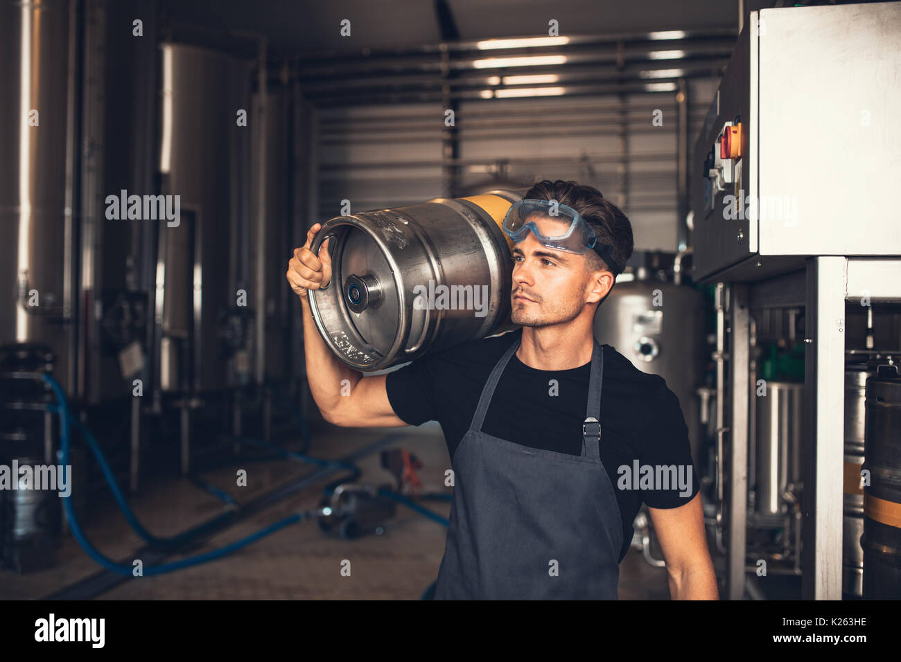 Brewer with large metal container at brewery factory. Young man working ...