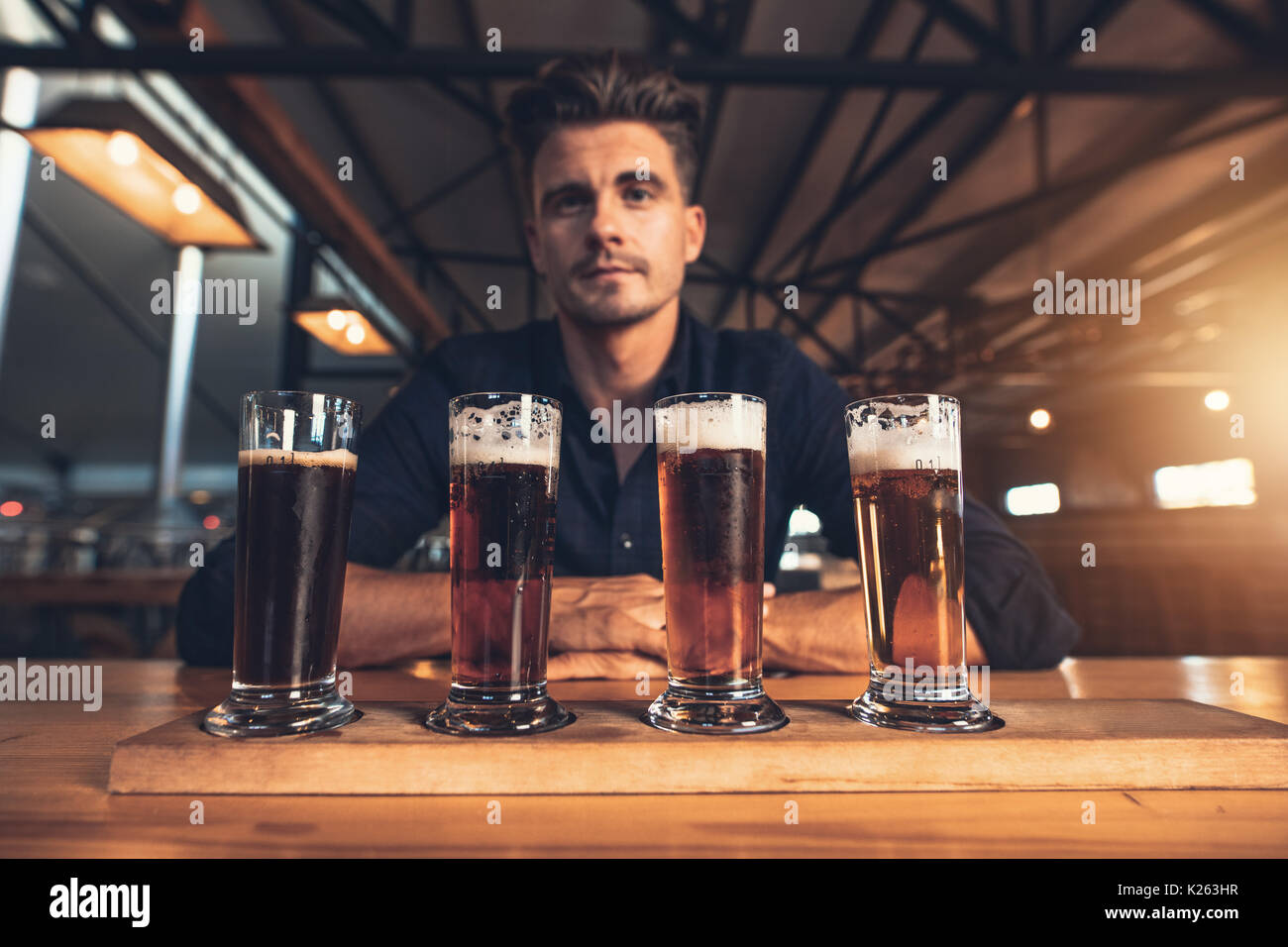 Young man tasting different varieties of craft beer on a wooden table ...