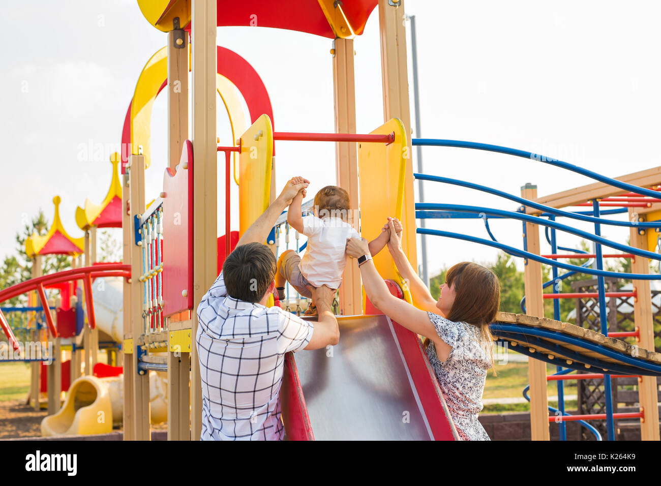 playful child with parents at the playground outdoor. Mom, dad and ...