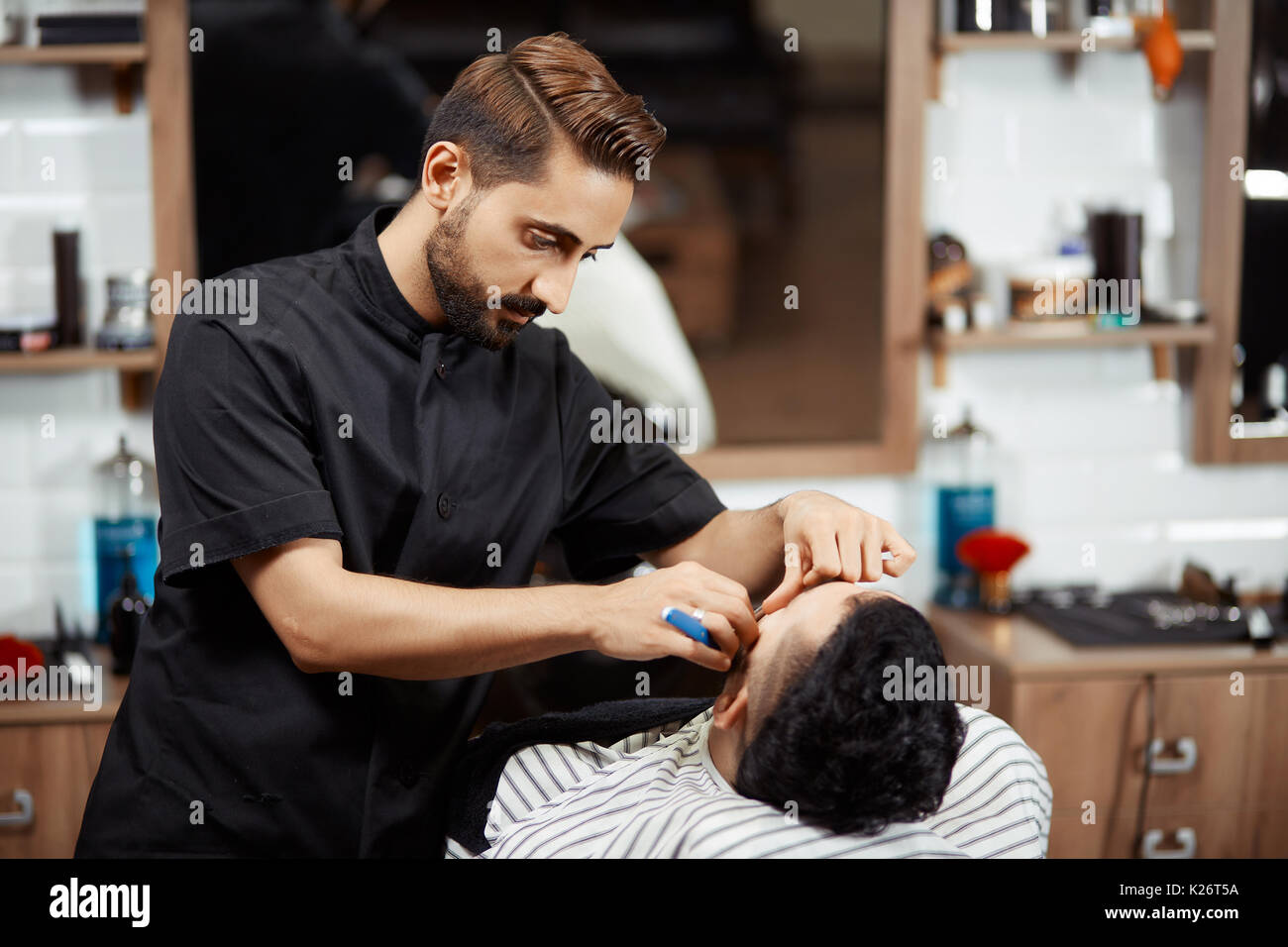 Hairstylist cutting bread of client in modern barber Stock Photo - Alamy