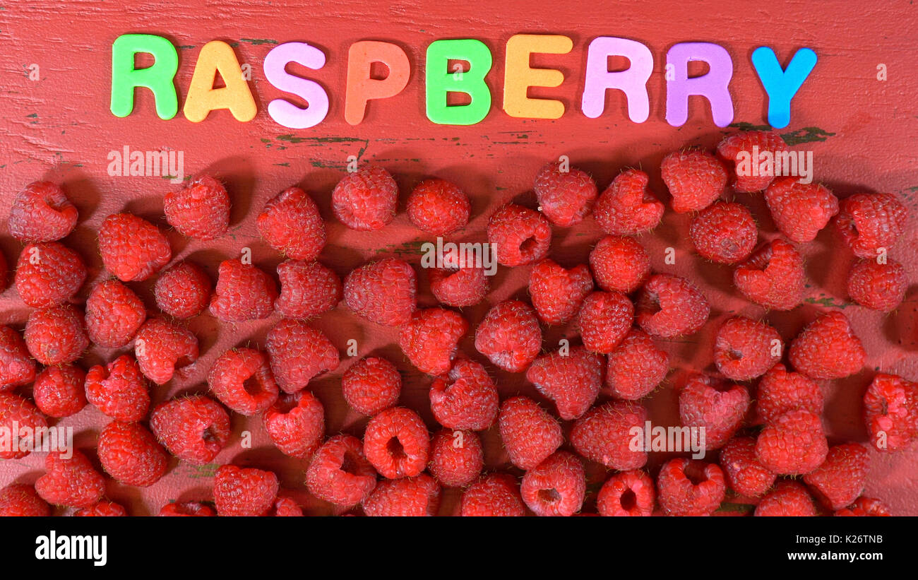 Raspberries on rustic red wood table background overhead with letters ...