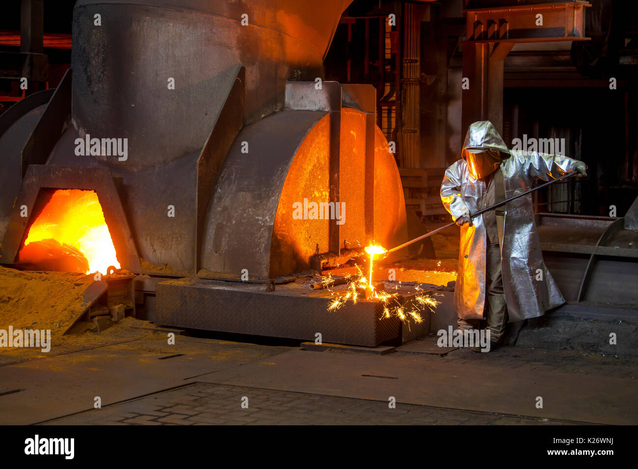 A steel worker in a protective suit taking a 1500 ° hot raw iron sample ...