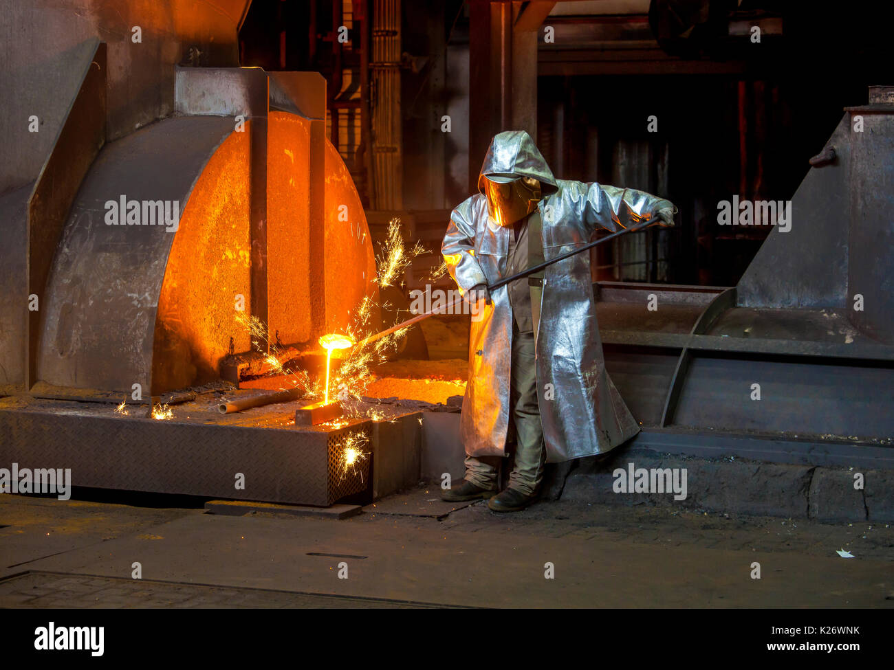 A steel worker in a protective suit taking a 1500 ° hot raw iron sample ...
