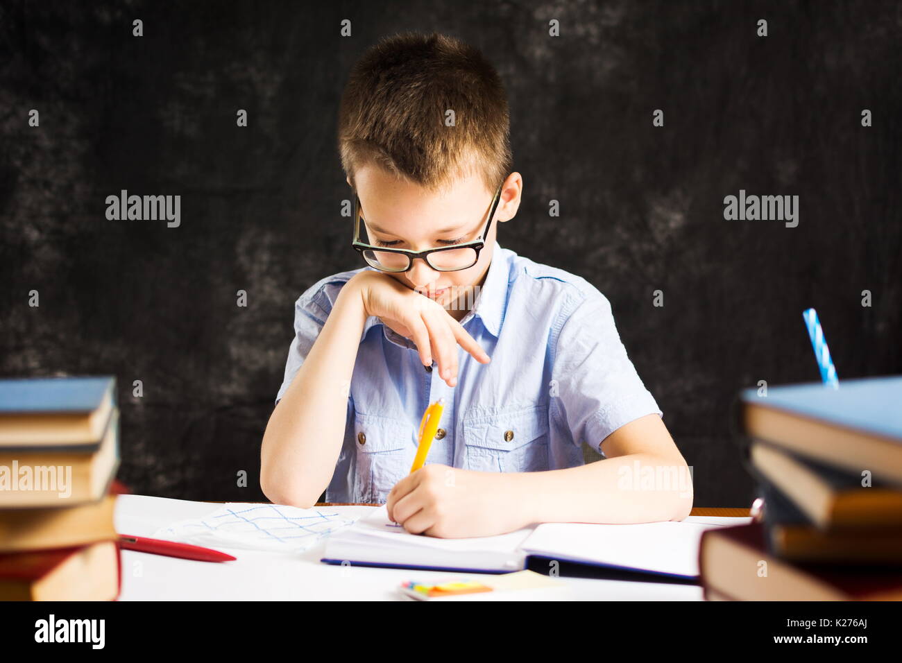 Boy writing in notebook on the desk covered with books Stock Photo - Alamy