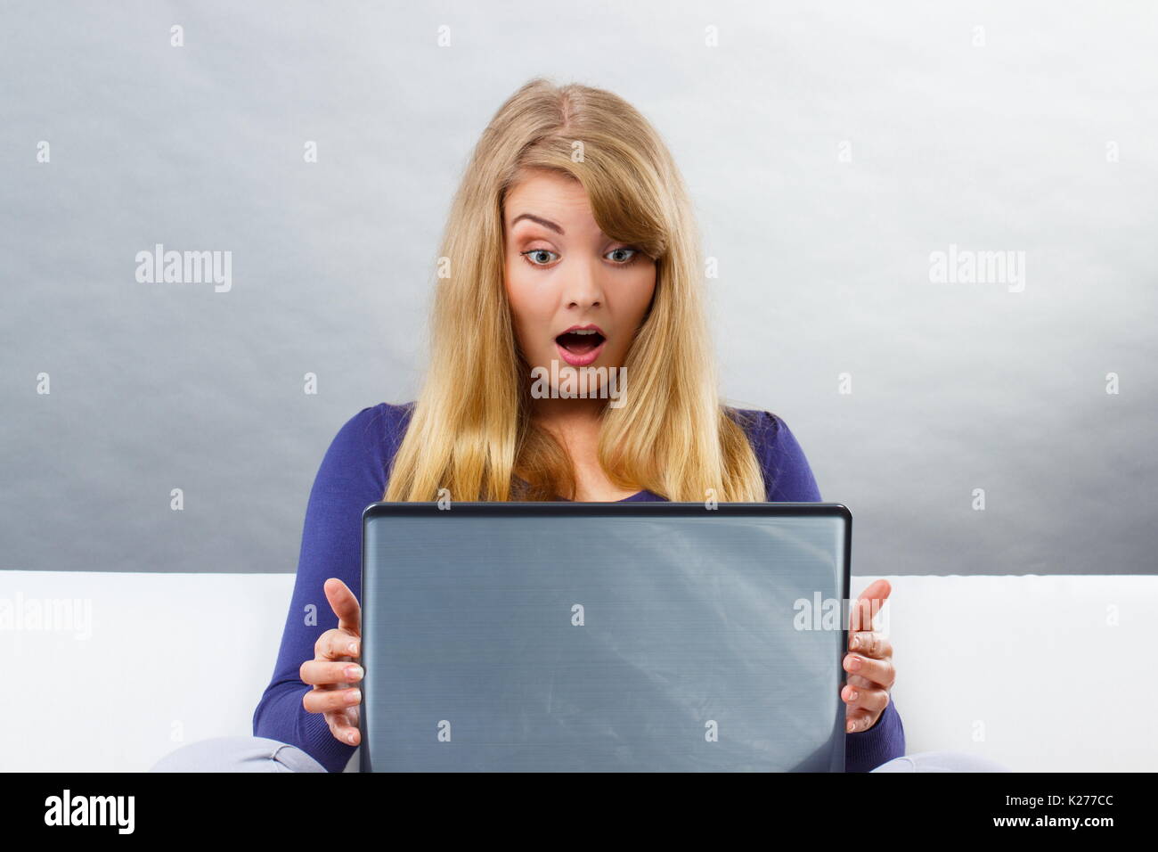 Surprised and scared woman sitting on sofa and looking at laptop screen ...