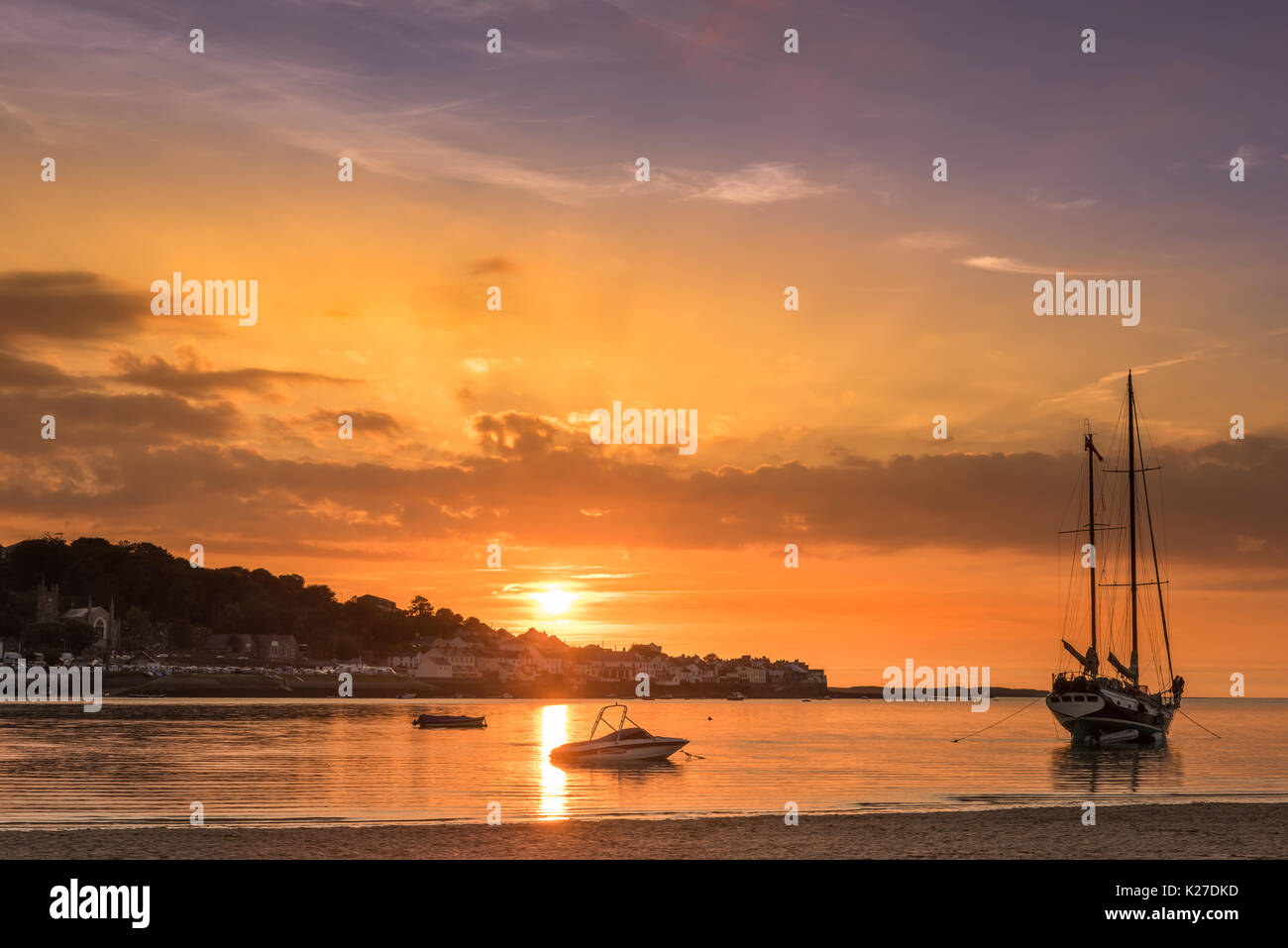 The sun sets behind the village of Appledore as the tide rolls up the ...