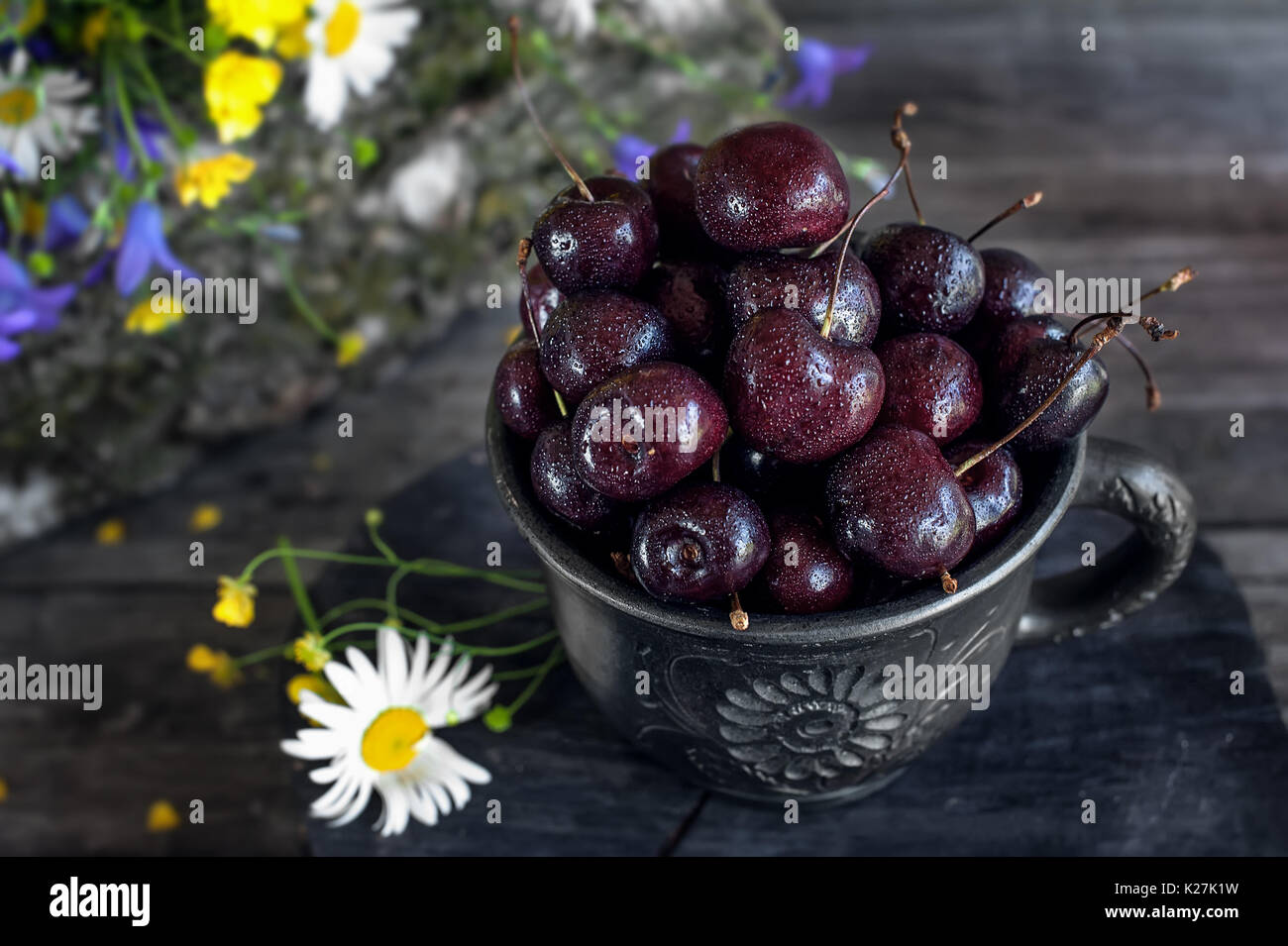 Ripe juicy cherries in a clay pot with field daisies and bells in a ...