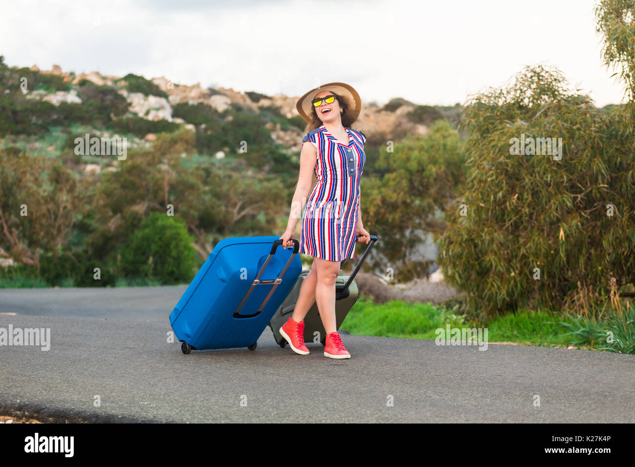 Happy cheerful traveler woman standing with suitcases on the road and ...