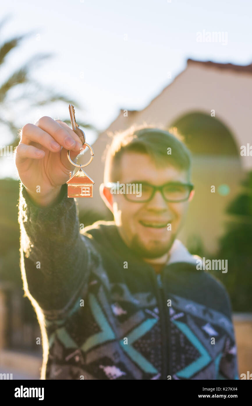 Young man holding house keys on house shaped keychain in front of a new ...