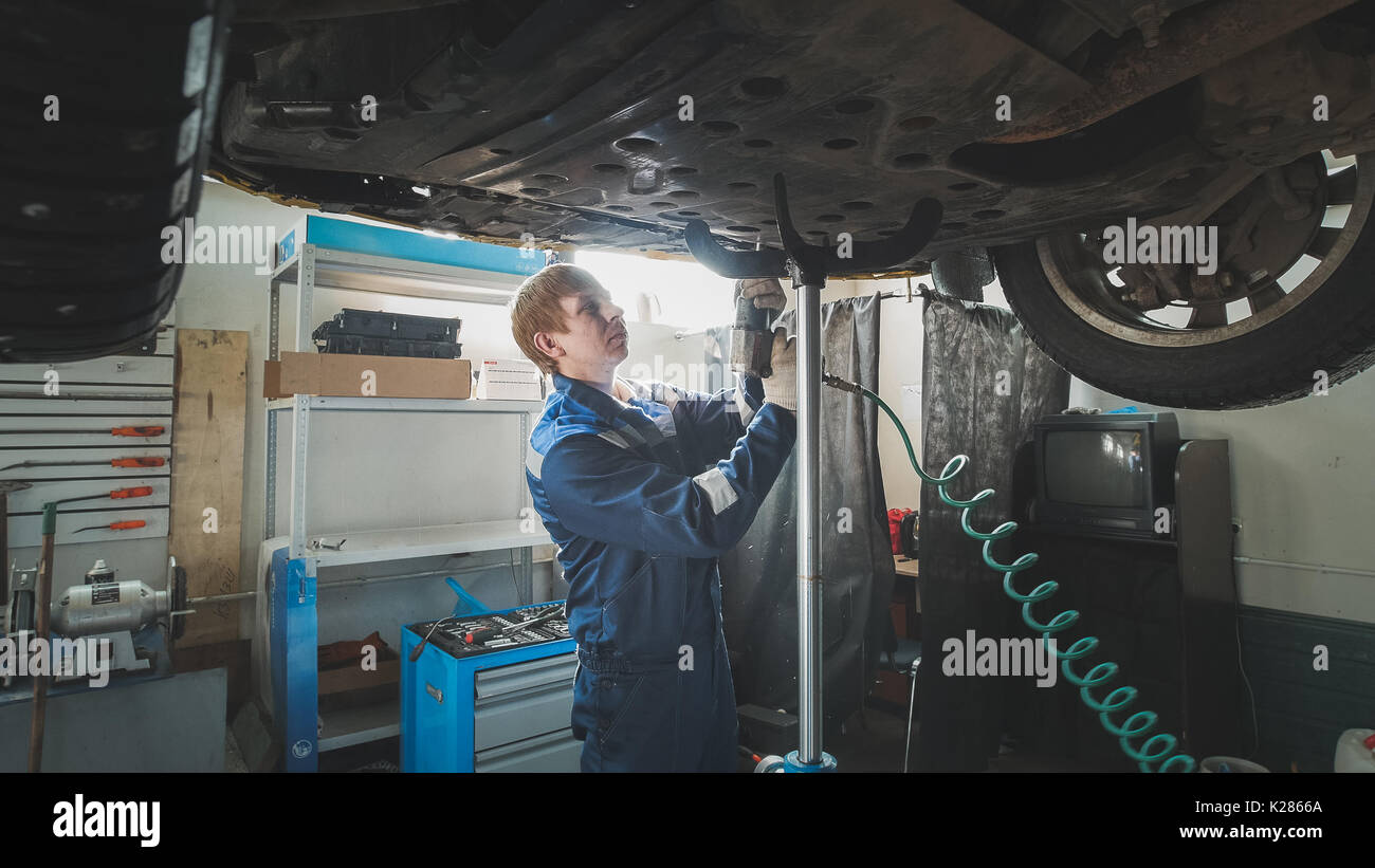 Worker Mechanic unscrewing parts of automobile's bottom under lifted ...