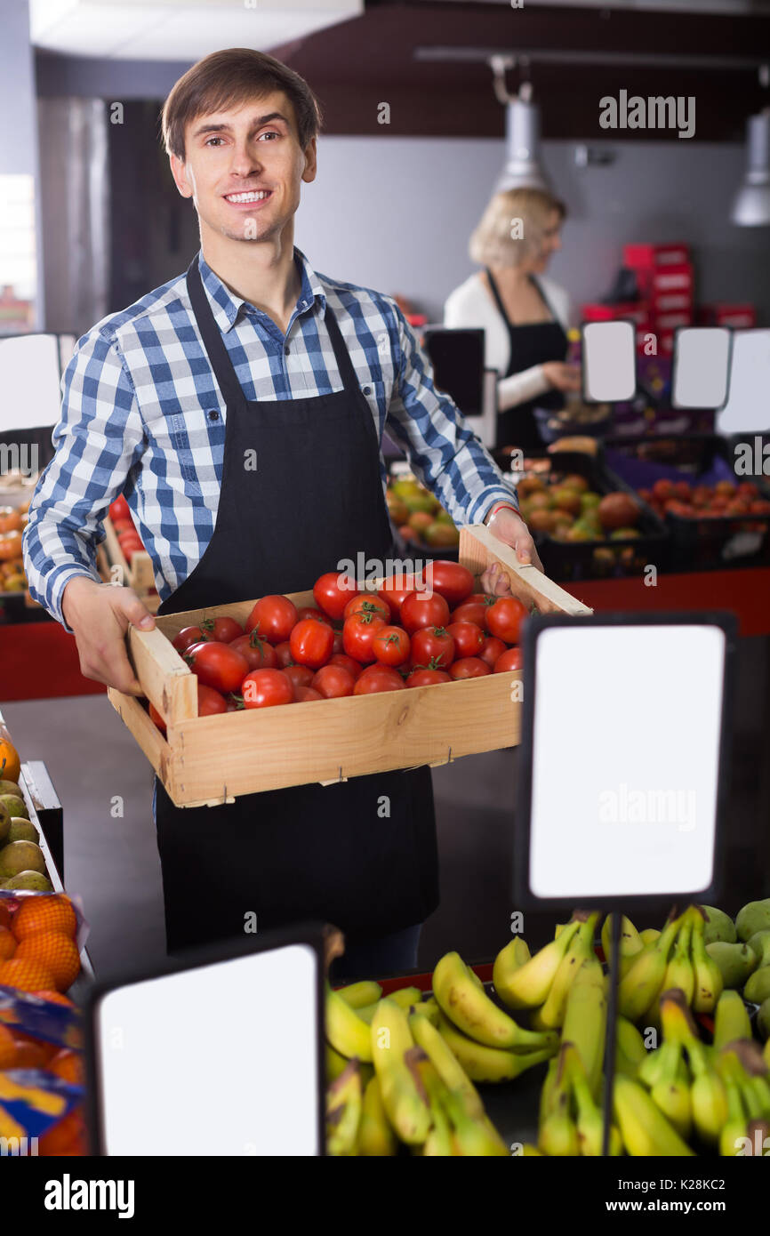 Positive employee of farm food store with fruits and vegetables Stock ...