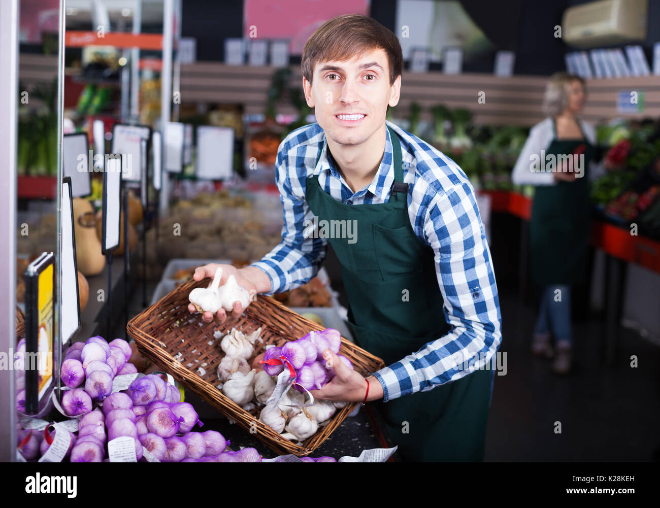 Positive grocery worker selling fresh garlic at local market Stock ...