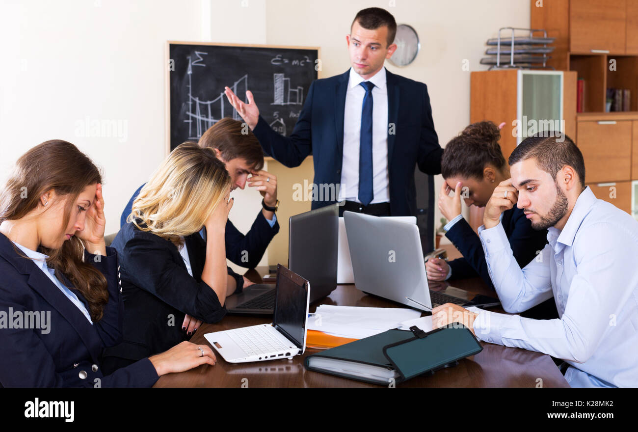 Disappointed young boss shouting at employees in office interior. Focus ...