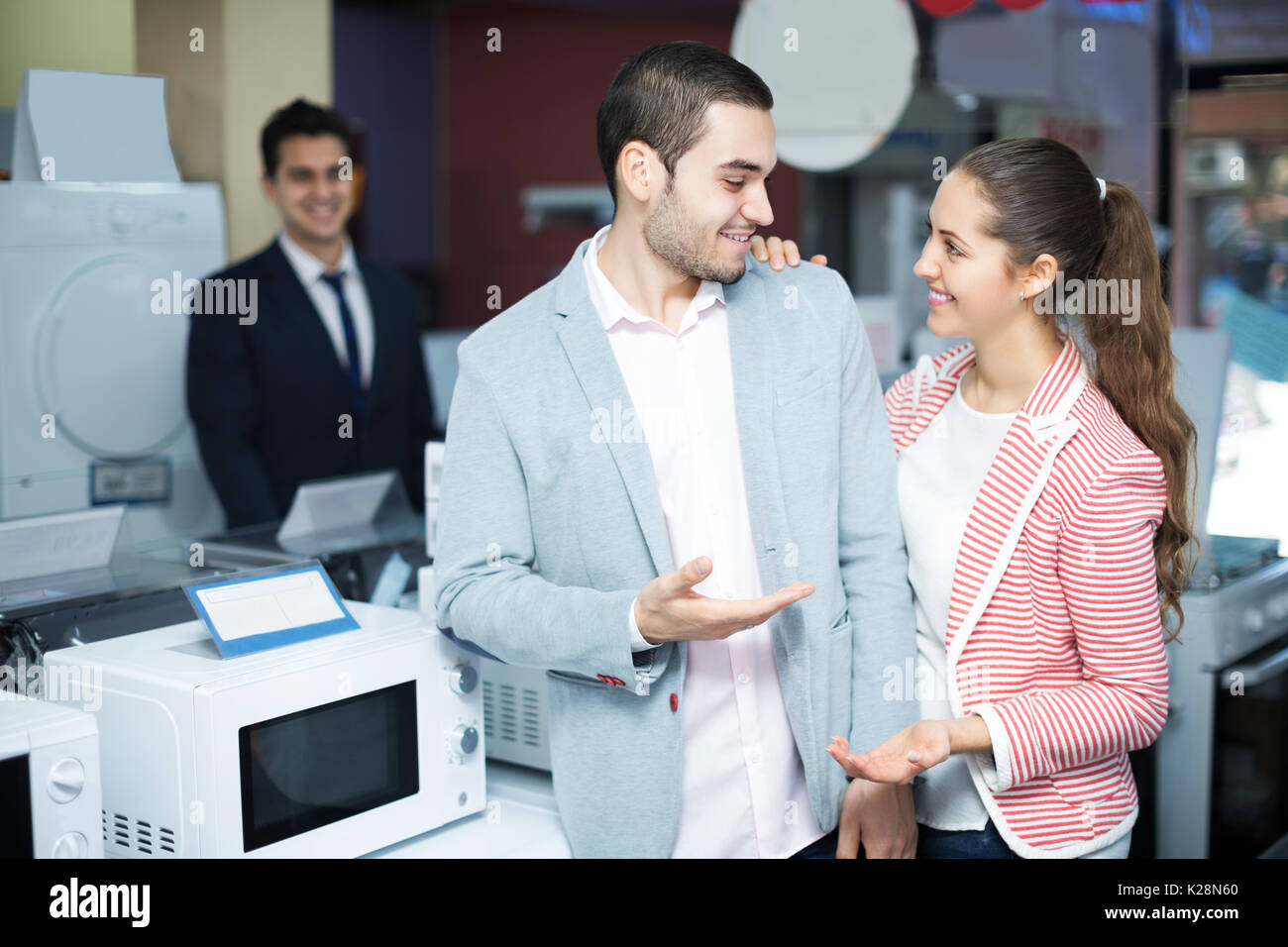 Experienced shop assistant helping positive young customers to choose ...