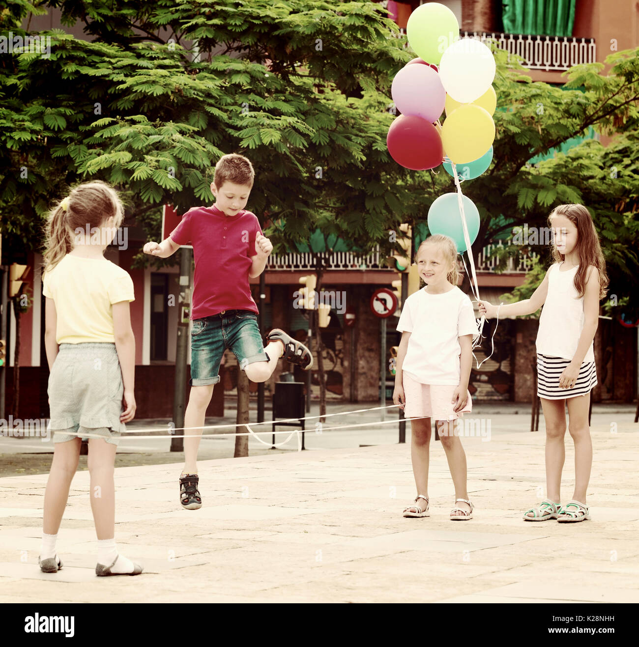 Boy skipping on chinese jumping rope and girls standing around with ...