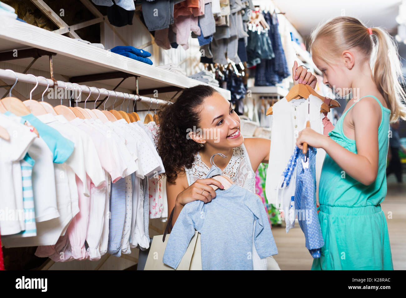 Mother with daughter buying kids clothes in blue color in shop Stock ...