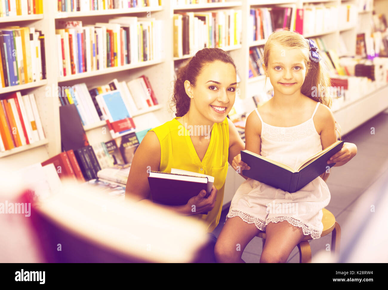 Portrait of positive young woman with girl reading textbook in book ...