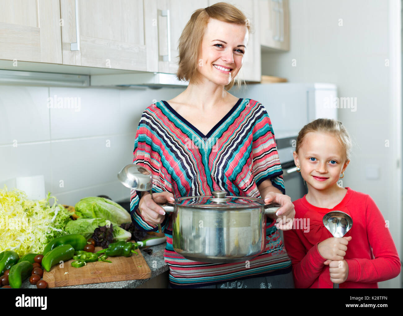 Portrait of smiling girl and mom with vegetables and pot in kitchen ...