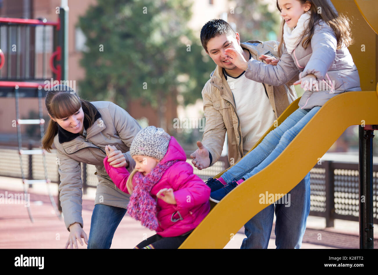 Smiling adult parents playing with little daughters at slide of ...