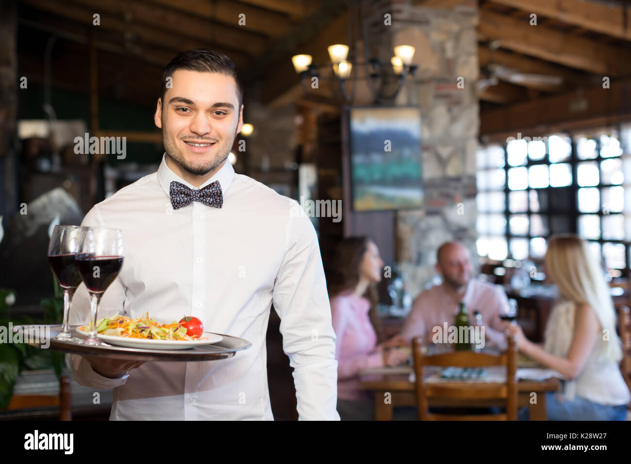 Smiling handsome waiter wearing a white shirt and a bowtie holding a ...