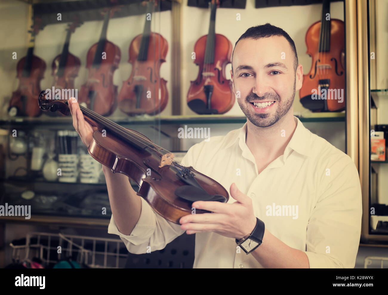 Happy male musician selecting classical violin in music instruments ...