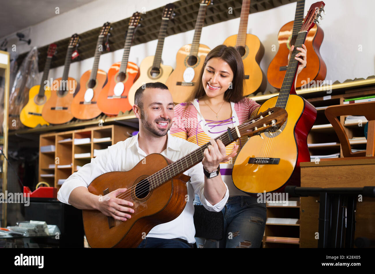 Smiling girl and handsome young guy playing the guitars in shop Stock ...