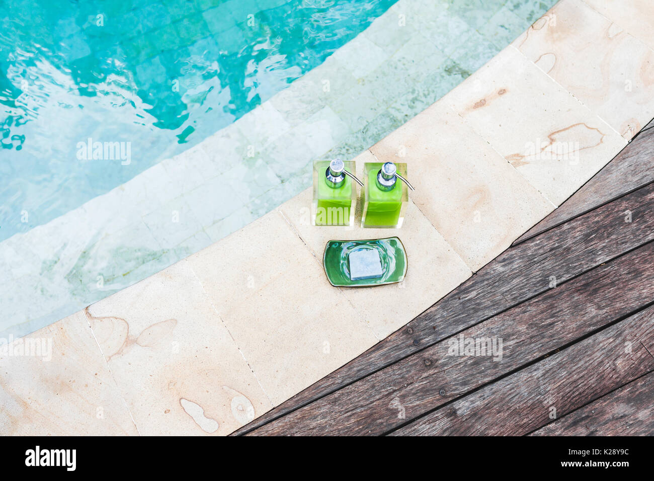 Two bottles of shampoo and handmade soap on edge of pool with turquoise ...