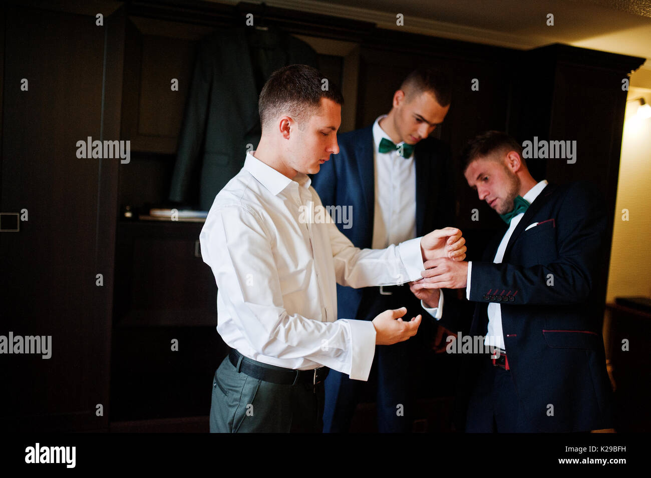 Groomsmen helping groom to dress up and get ready for his wedding ...