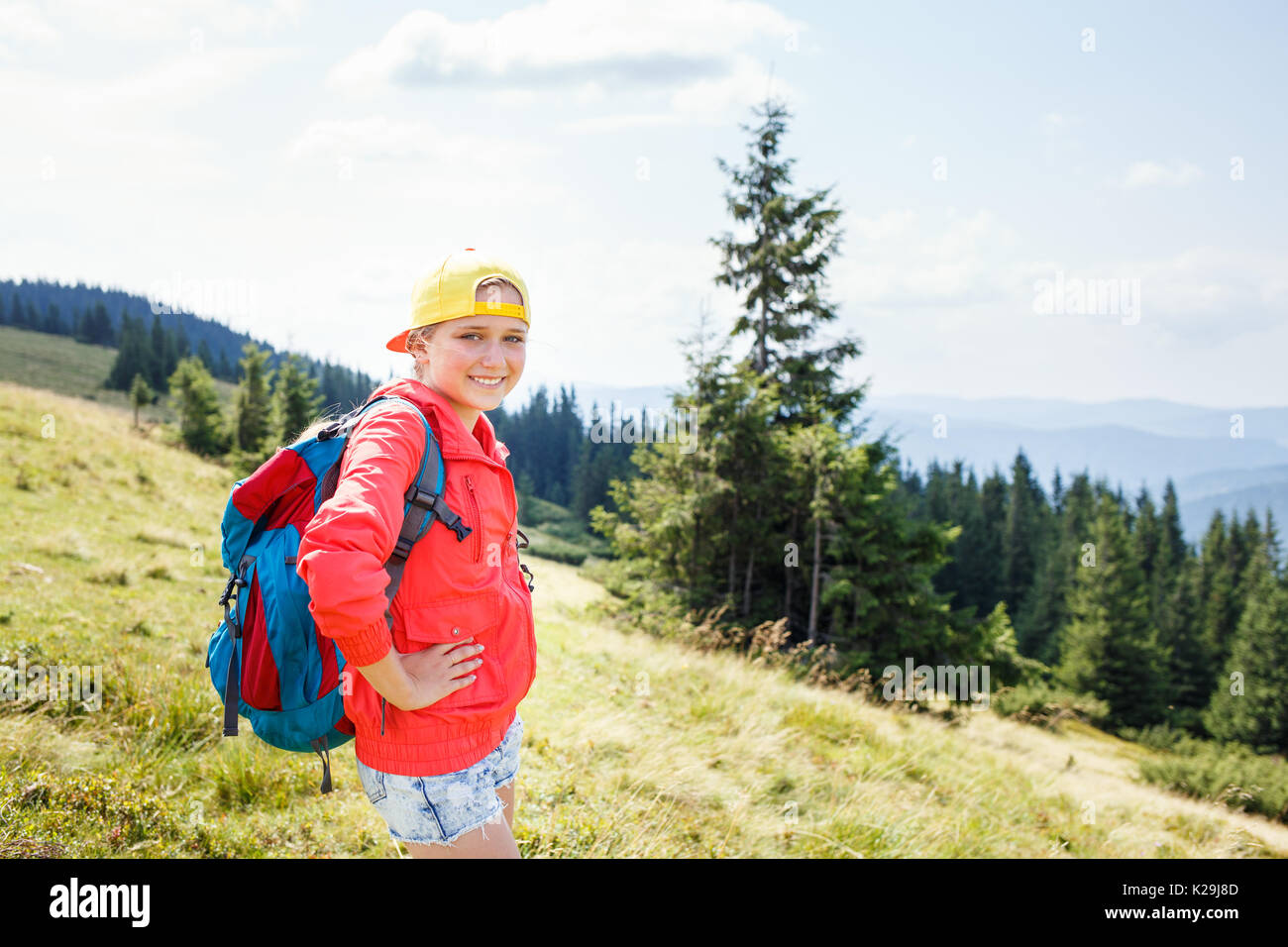 Young smiling teenage girl with backpack enjoying view in mountains ...