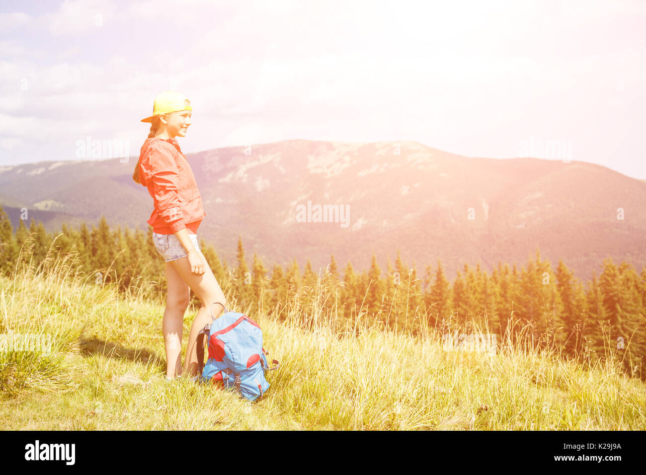 Young smiling teenage girl with backpack enjoying view in mountains ...