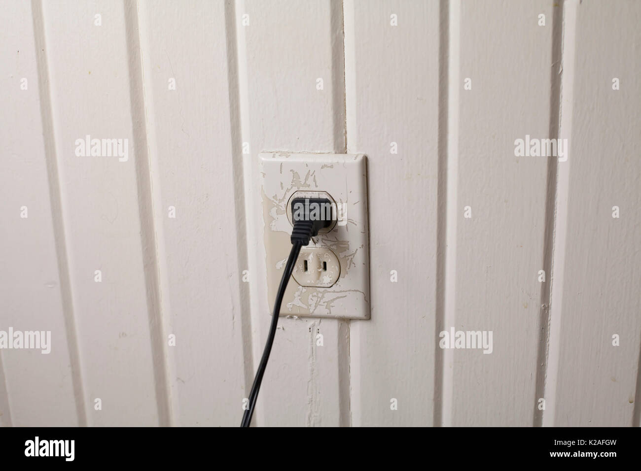 Black cord plugged into an outlet on an off-white wall Stock Photo - Alamy