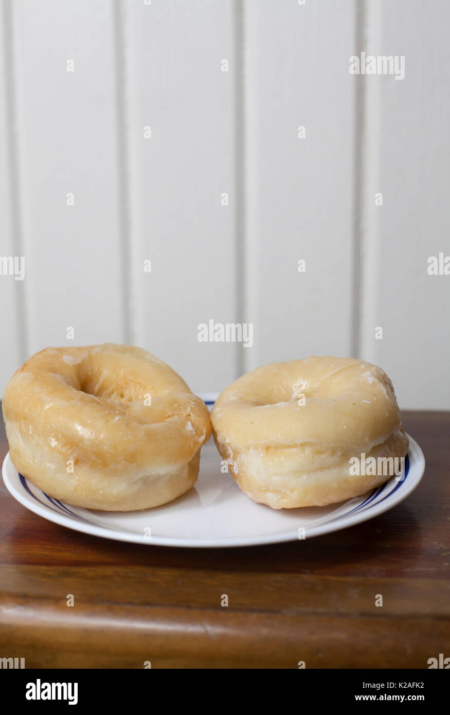 Two sweet, glazed donuts on a serving plate Stock Photo - Alamy