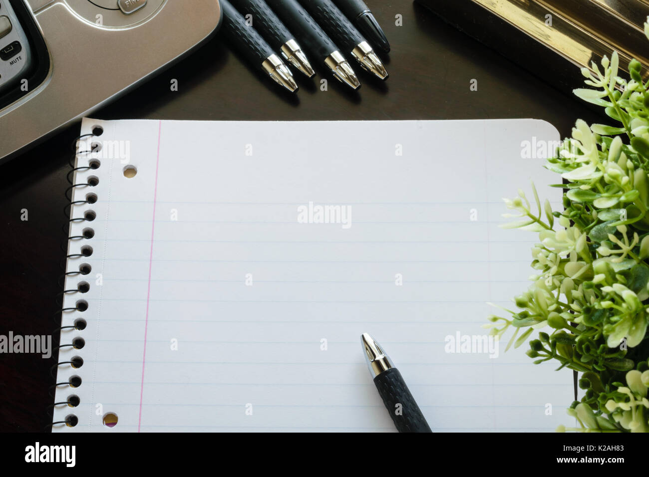 Blank lined paper and pen on wooden desk with phone, flower and the ...