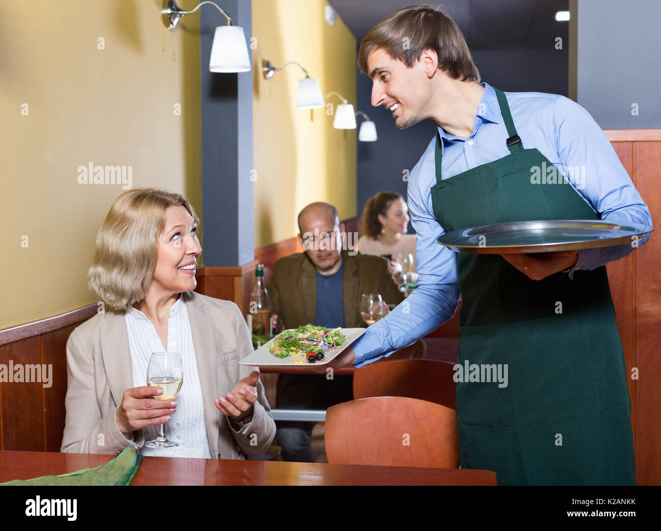 Positive waiter bringing order to happy smiling mature female in ...
